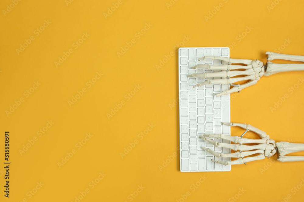 Human skeleton using computer keyboard on yellow background, top view ...