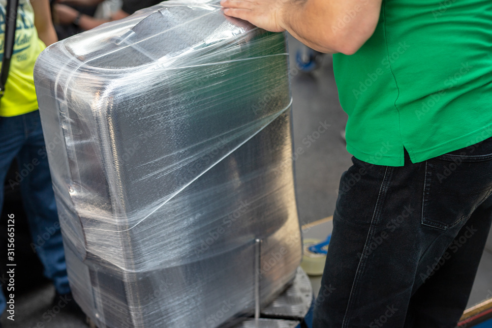 Foto de Worker wrapping suitcase with transparent protection film ...