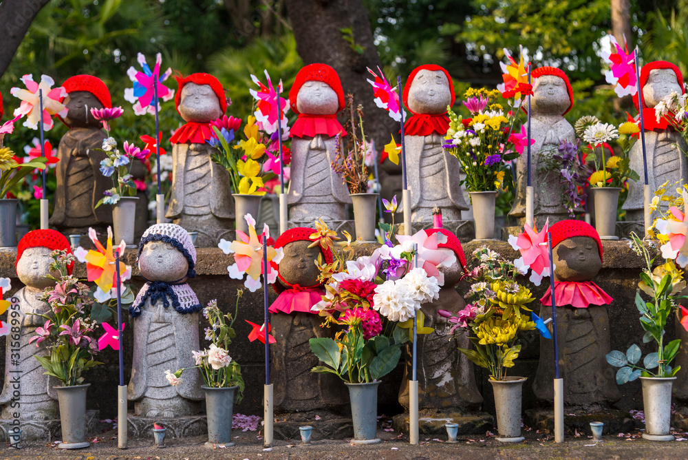 Rows jizo statues with red bibs, hats, flower and colorful wind mills ...