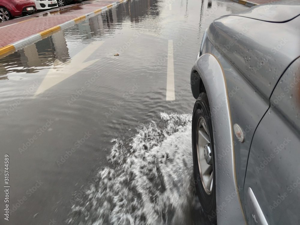 splashing water by driving SUV wheels in rain flooded water in parking ...