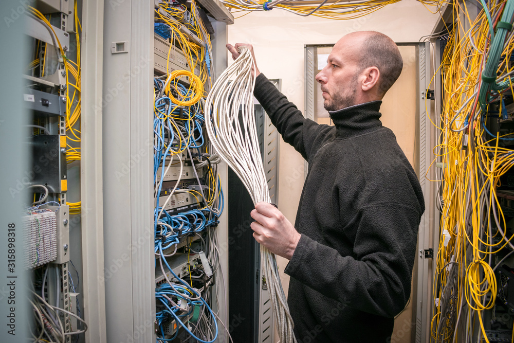 Technology Concept. A man works with communication cables in a data ...