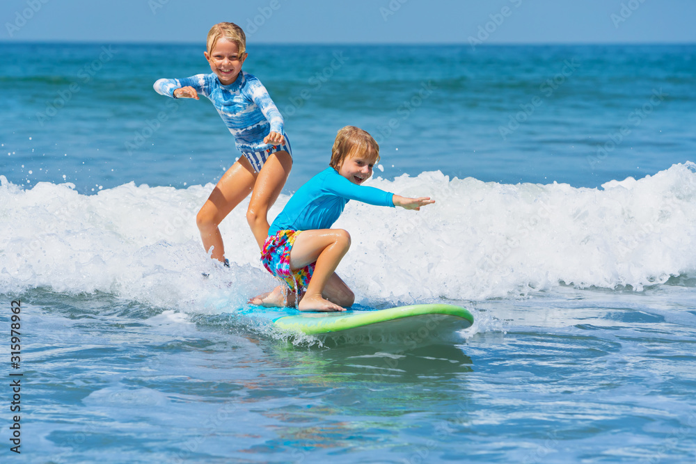 Happy baby boy and girl - young surfers ride with fun on one surfboard ...
