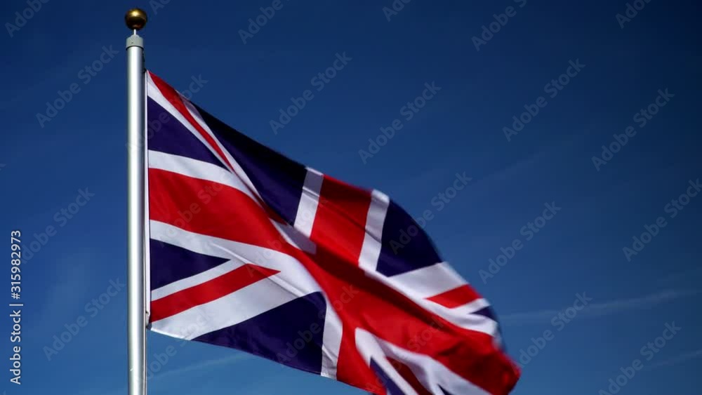 UK Union Flag flying in the wind outdoors with Blue sky behind ...