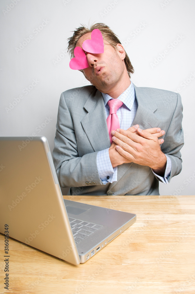 Lovestruck businessman sitting swooning at his desk with hearts in his ...