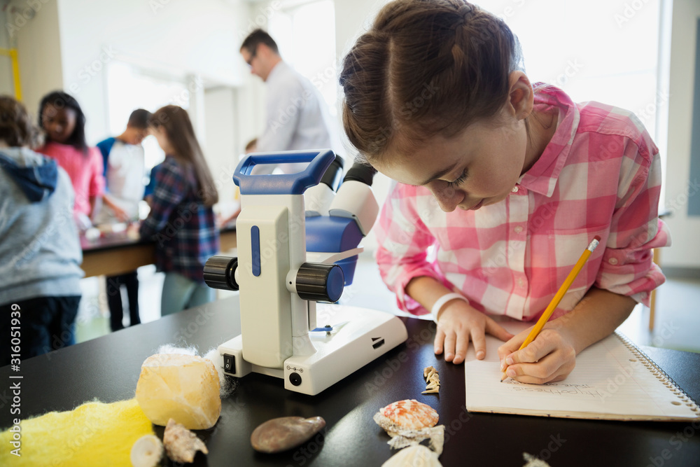Schoolgirl taking notes at microscope science laboratory classroom ...