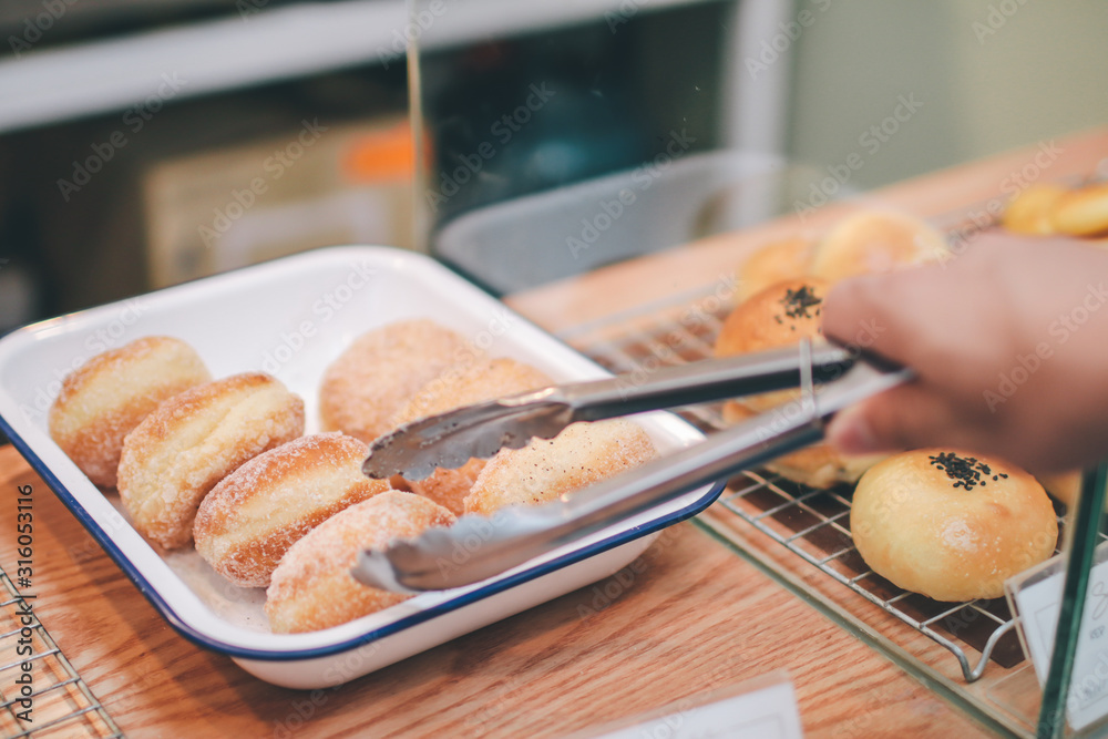 Closeup of woman holding clamp picking sugar-glazed doughnuts a bakery ...