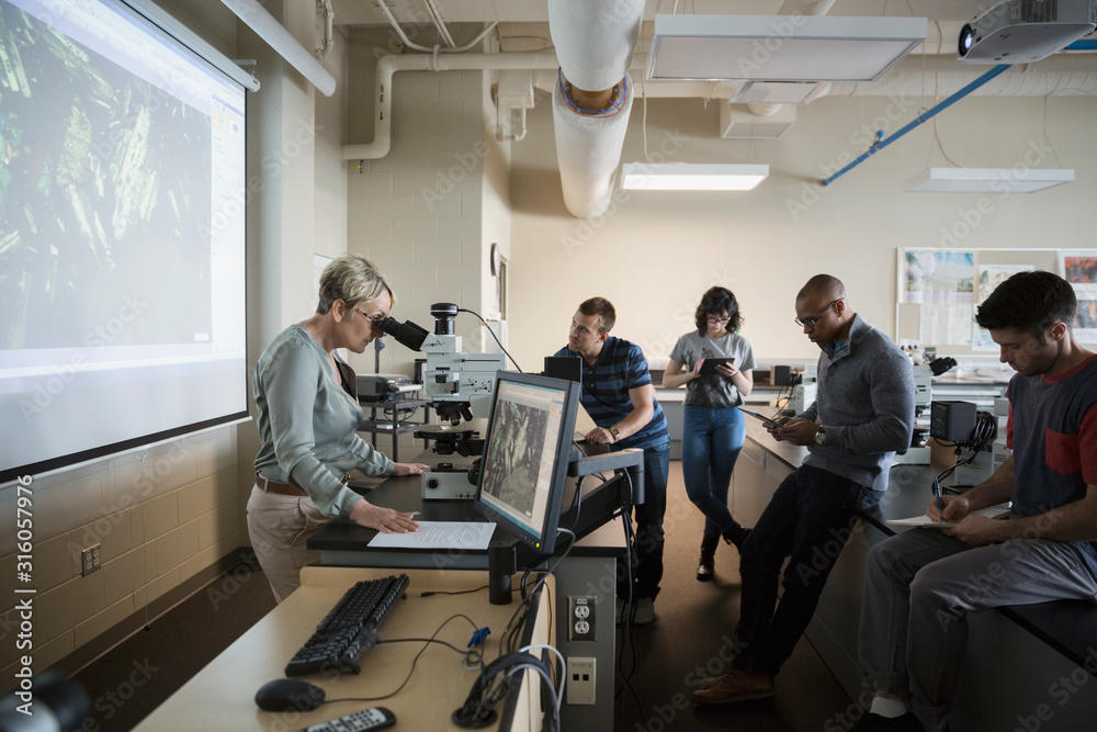 Science professor at microscope leading lesson in classroom Stock Photo ...