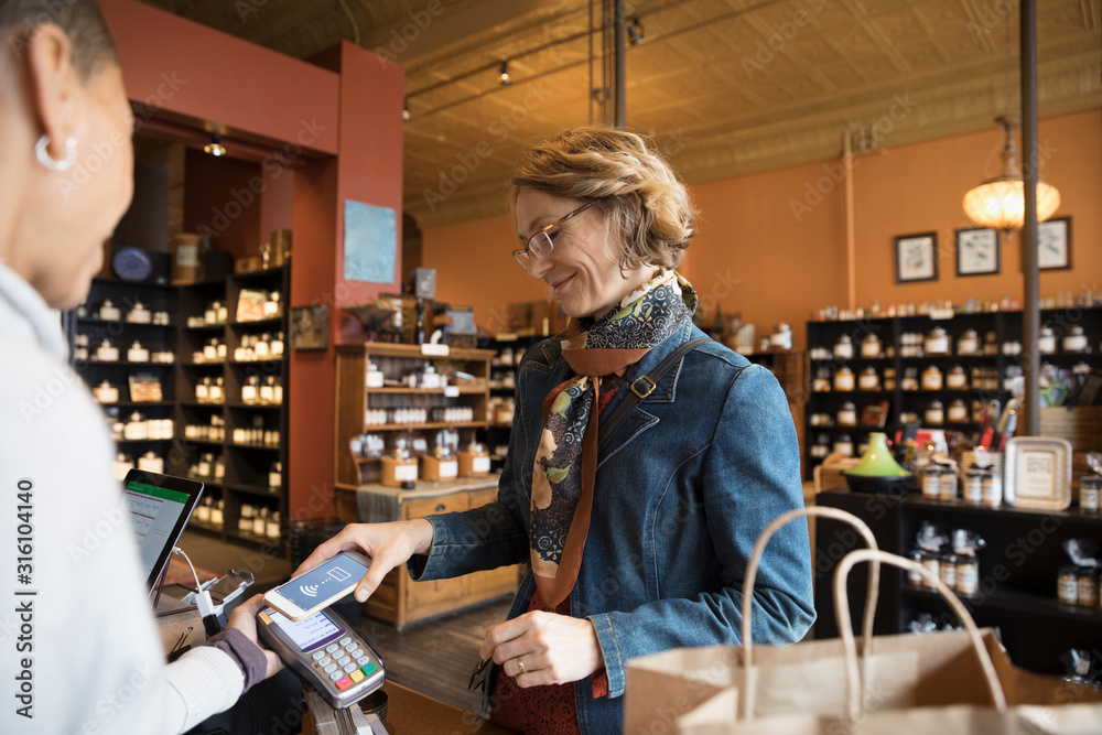 Female customer using smart phone contactless payment at shop counter ...
