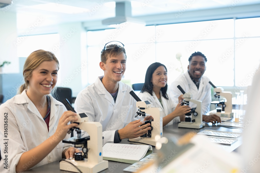 Smiling college students using microscopes, conducting scientific ...