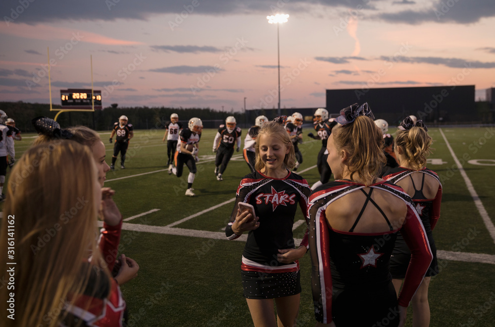 Teenage girl high school cheerleading team talking on sideline of game ...