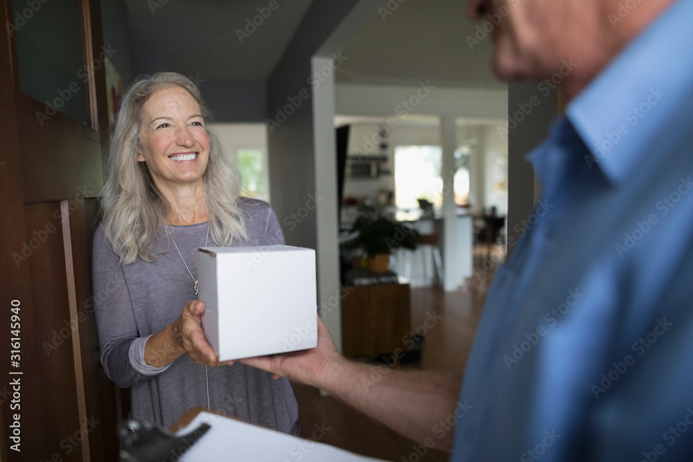 Smiling senior woman receiving box package from delivery man at front ...