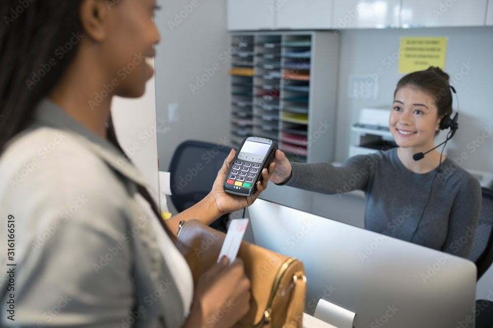 Clinic receptionist giving credit card swiper to patient at reception ...