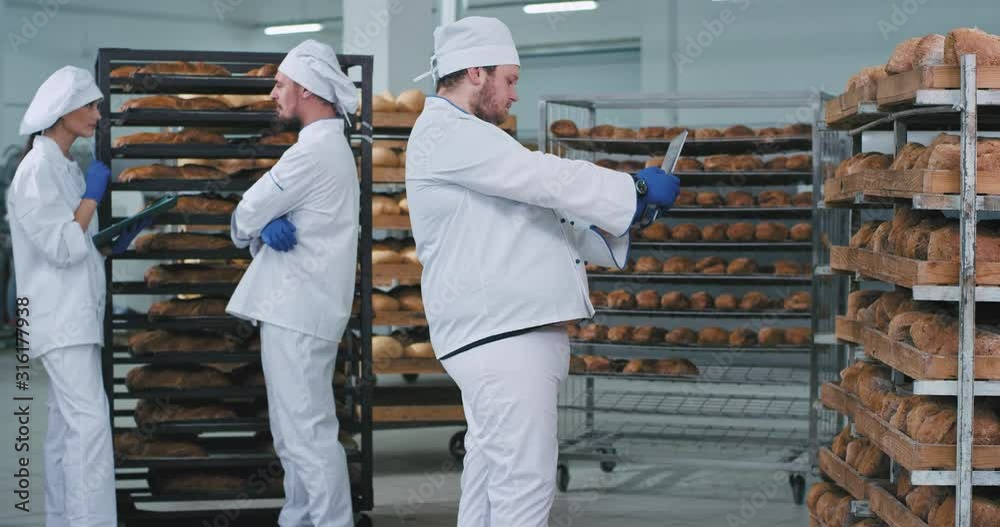 Group of bakers in a bakery stand up beside of full shelves of fresh ...