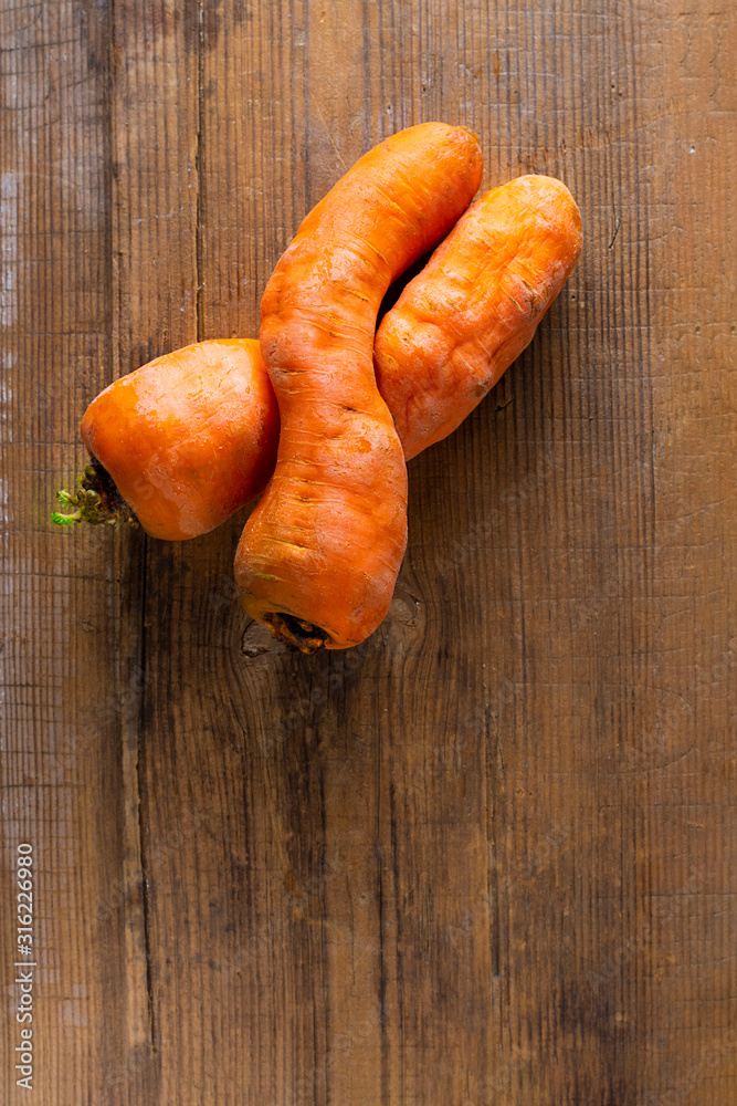 Two curved ugly carrots on brown old wooden background with copy soace ...