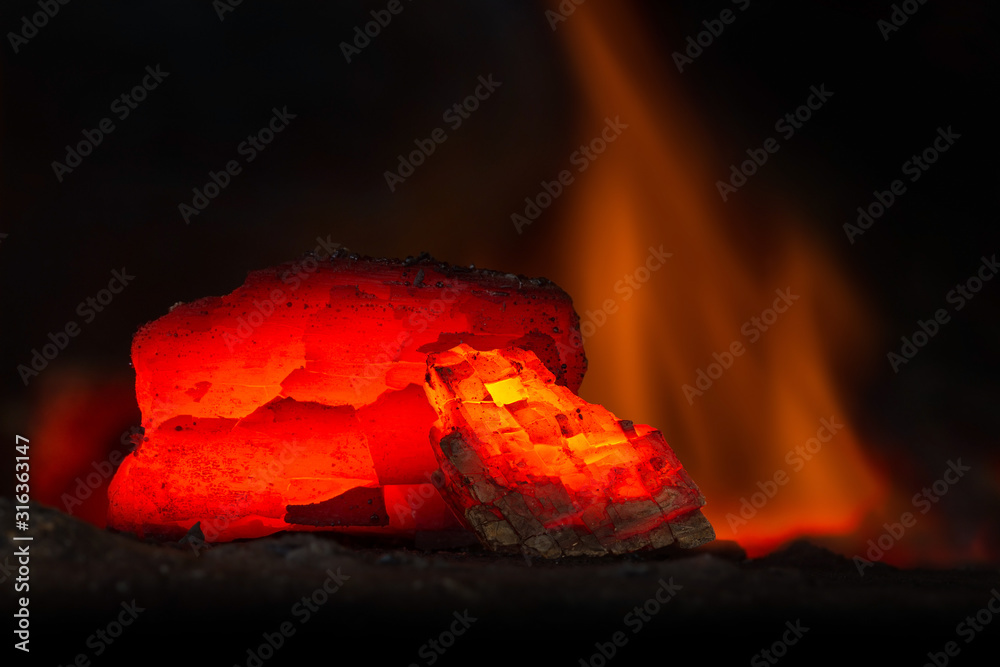 Red hot coal bars in focus on dark background with flames close up ...