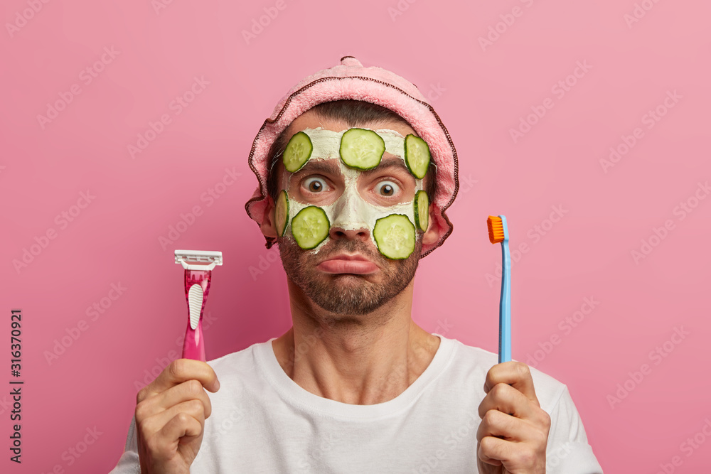 Puzzled man applies nourishing cleansing mask, holds toothbrush and ...