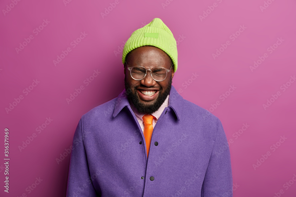 Fashionable guy with black healthy skin, laughs out as hear comic funny ...