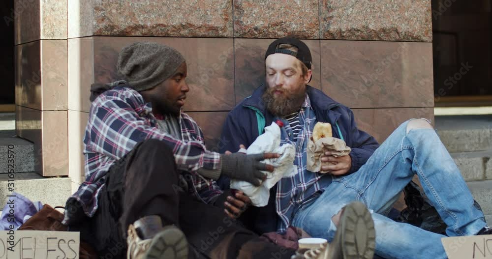 Two mixed-races young homeless poor men siting on the ground at the ...