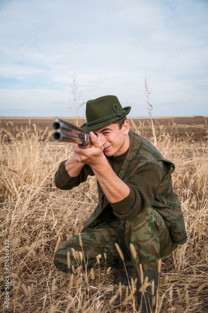 Caucasian hunter wearing green suit and hat kneels on his knee and ...