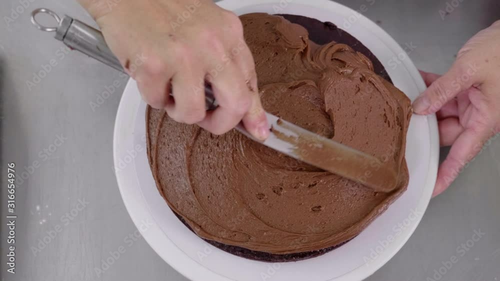 Top down shot of chocolate cake being topped with butter cream. The ...
