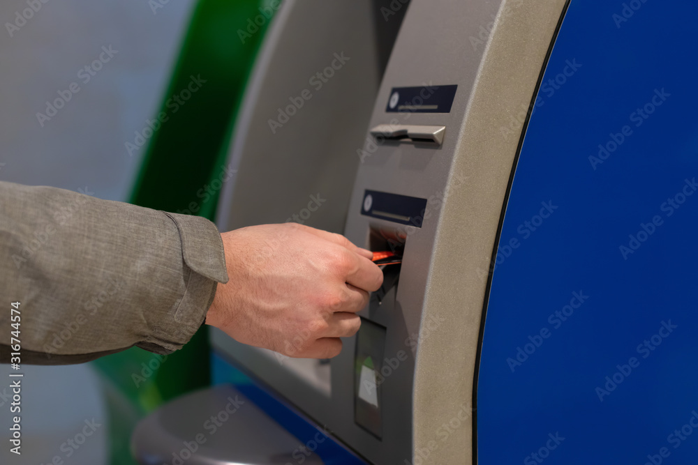 A male hand inserts a credit card into an ATM. Hole for a plastic card ...