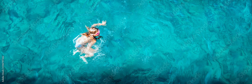 Young girl in swimwear lying on blue water. Kidn in swimming mask ...