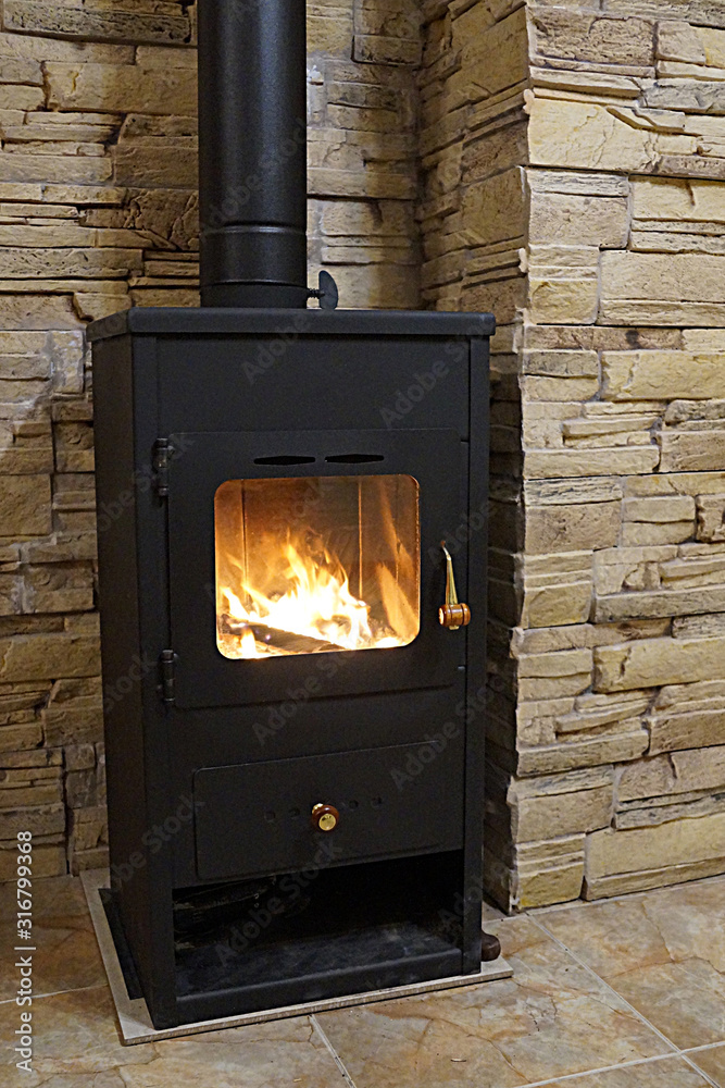 metal stove fireplace with fire behind glass in the interior against ...