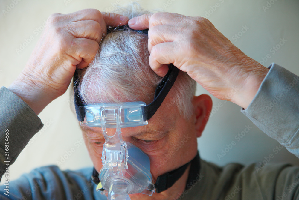 Older man puts on CPAP device head gear Stock Photo | Adobe Stock