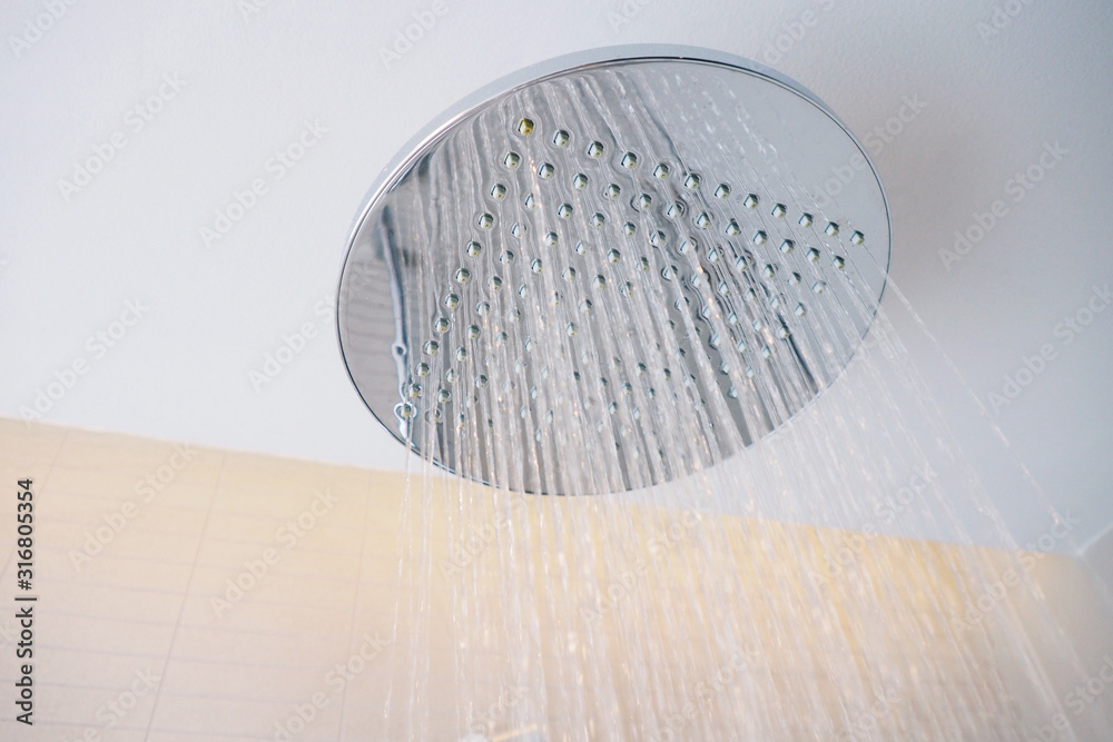 Water falling from modern stainless steel rain shower installed on the ...