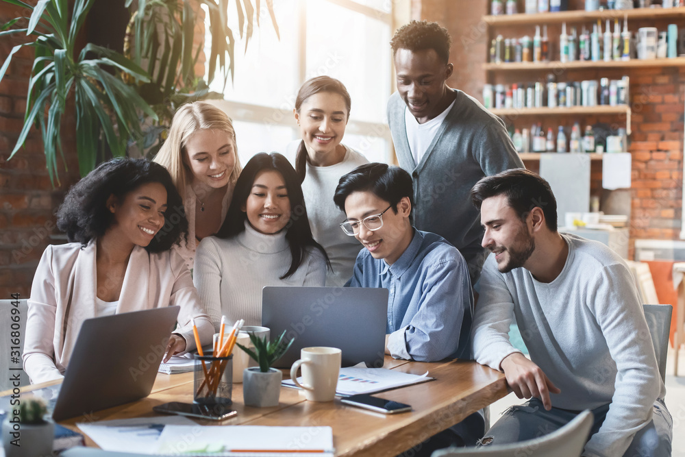 Excited international team looking at notebook screen, watching ...