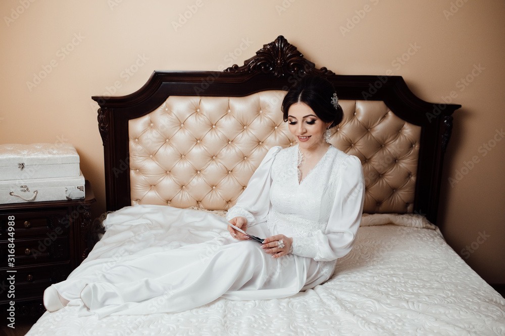 Luxury bride in white robe sittind in a bed in a luxury room while ...