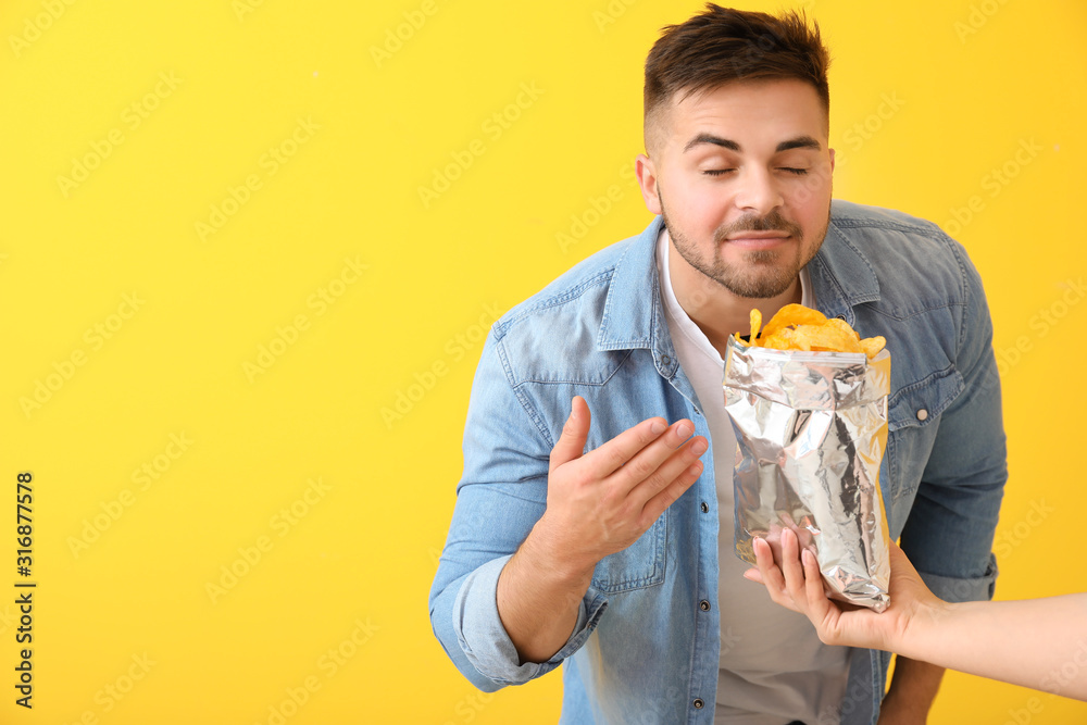Handsome young man and hand with tasty potato chips on color background ...