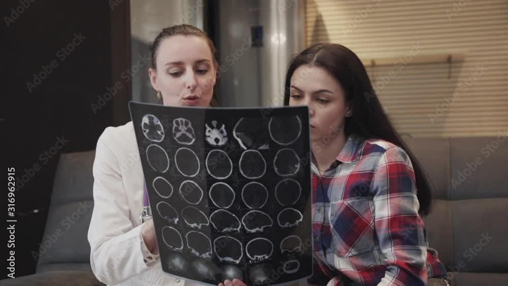 Young woman doctor and patient discussing x-ray sitting on sofa in ...