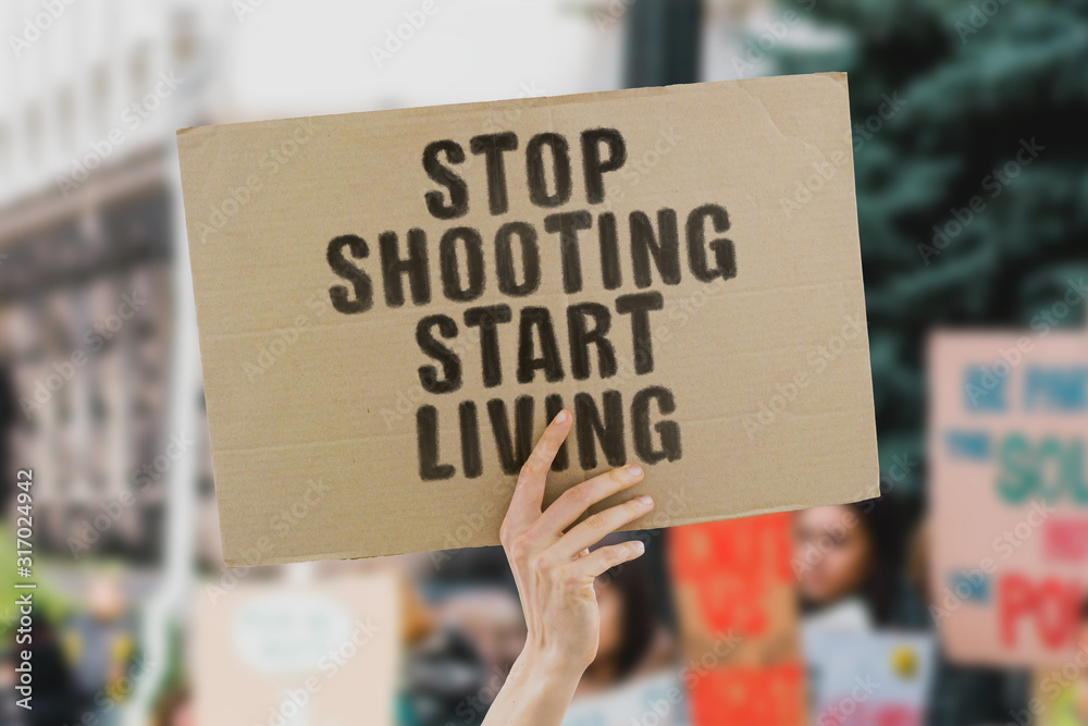 The phrase " Stop shooting start living " on a banner in men's hand ...