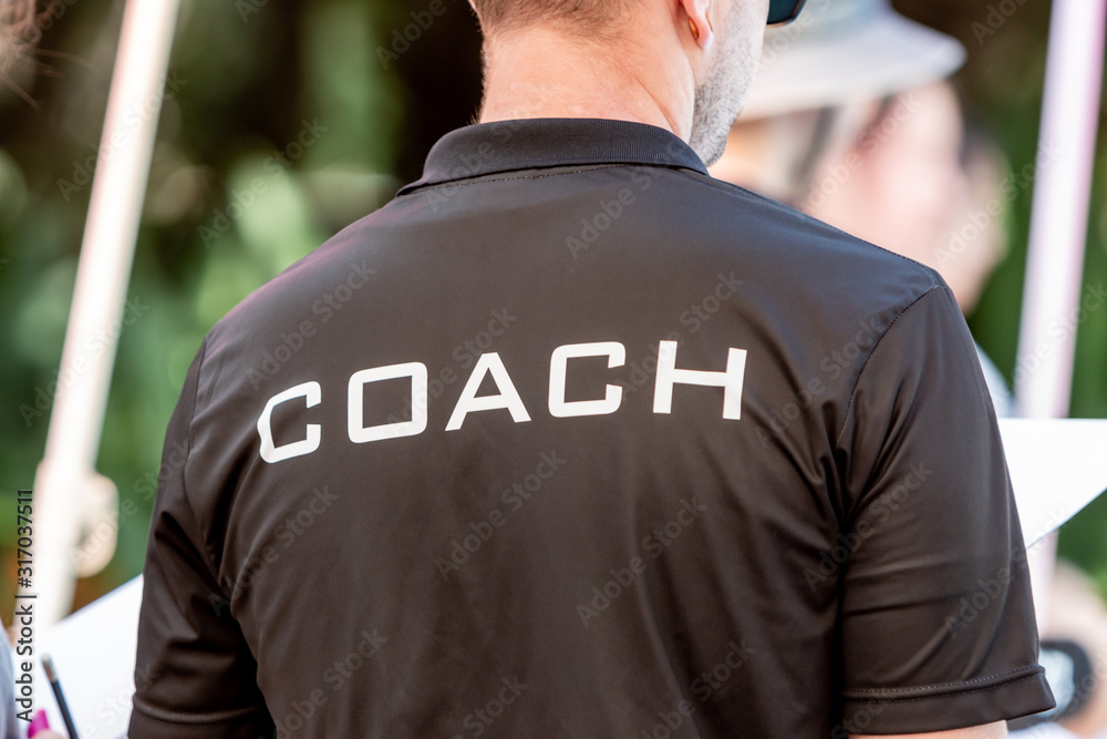 Back view of a male coach wearing black coach shirt with the white word ...