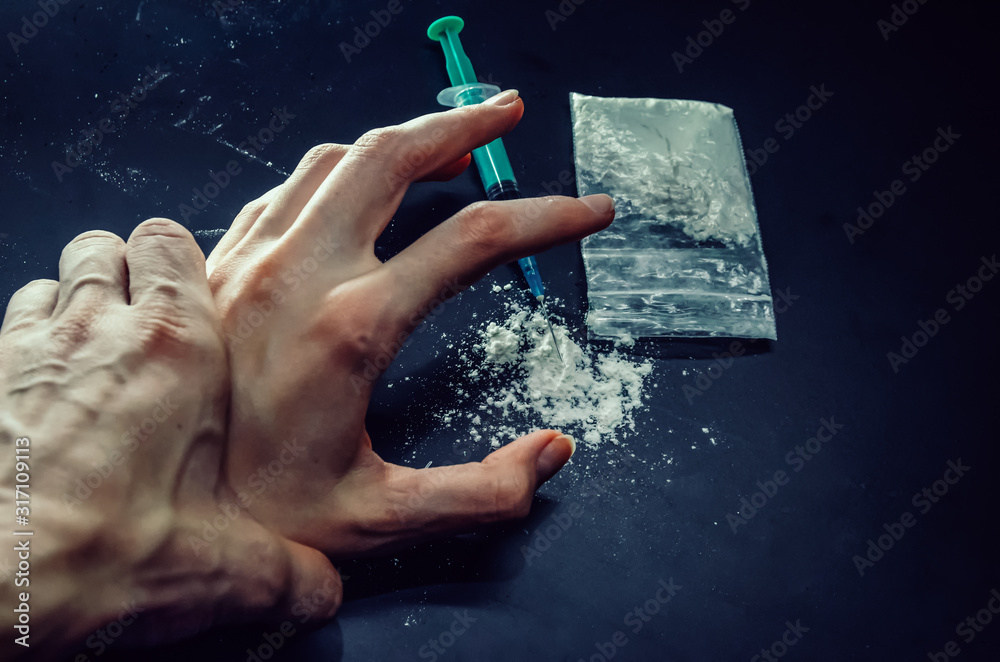 Hand grabs the hand of a drug addict with a package of drugs, a syringe ...
