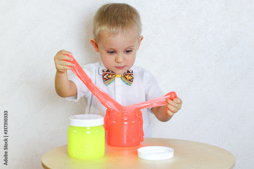 A little toddler boy is intently playing with slime, a sensory play ...