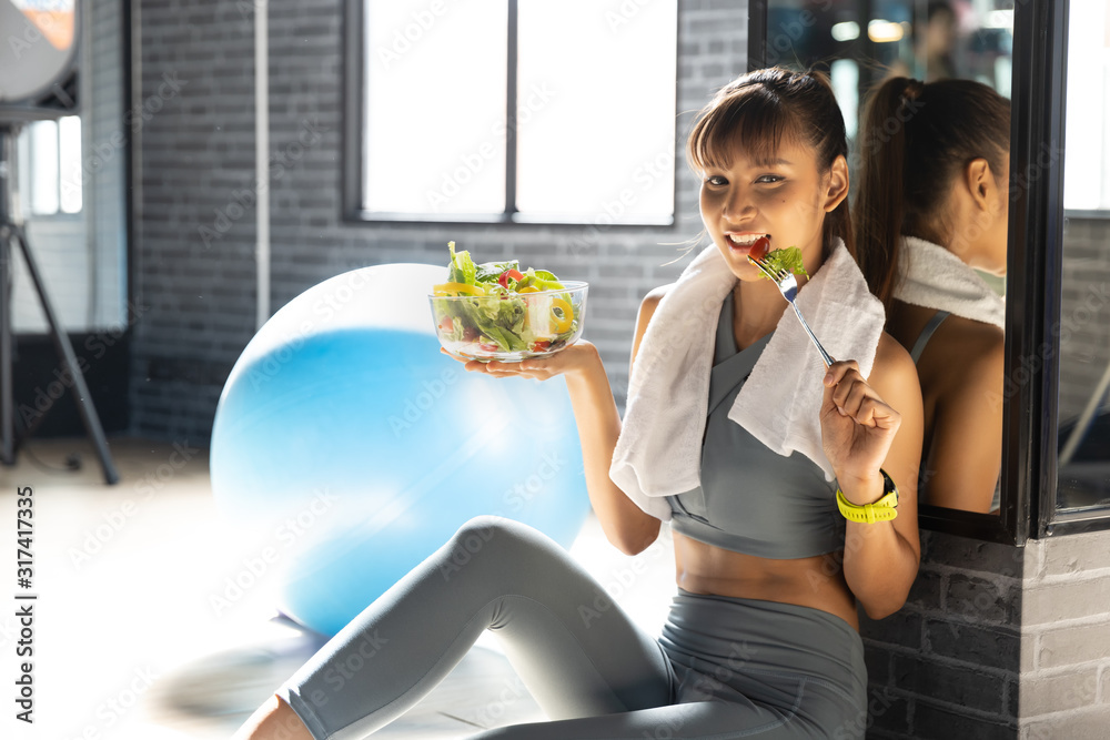 Healthy asian young woman eating vegetables green salad at gym In a ...