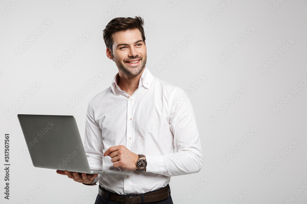 Image of young cheerful businessman holding and using laptop foto de ...