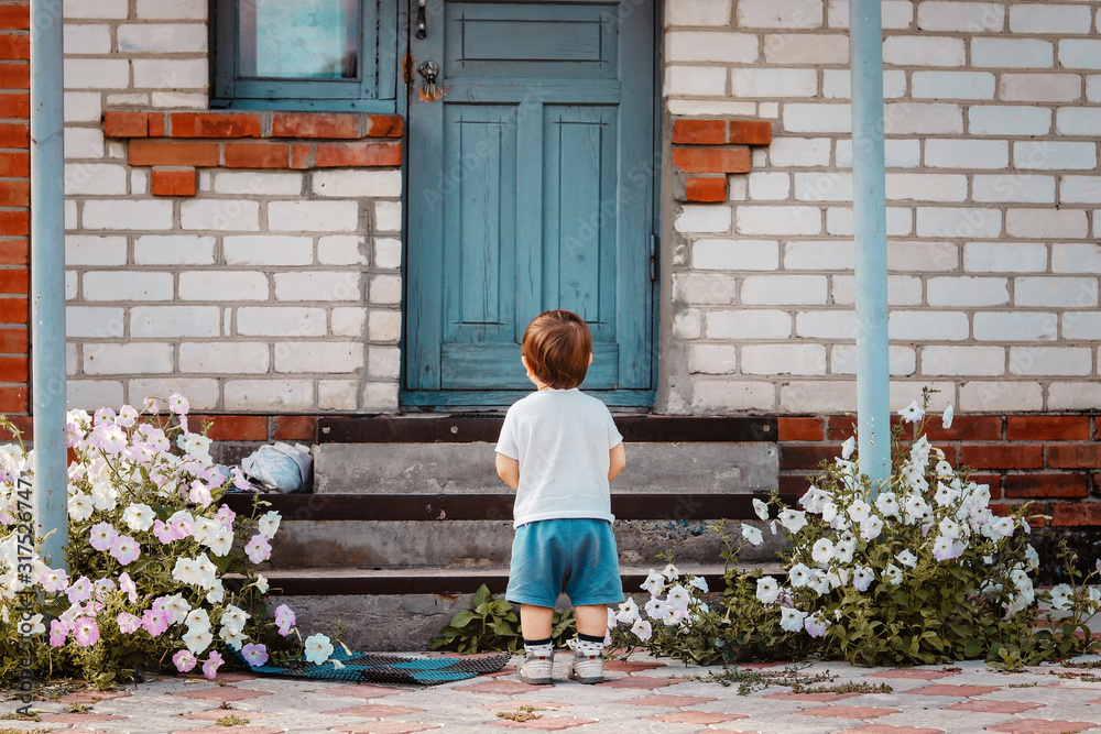 Back view of cute lonely little boy standing outside in front of blue ...