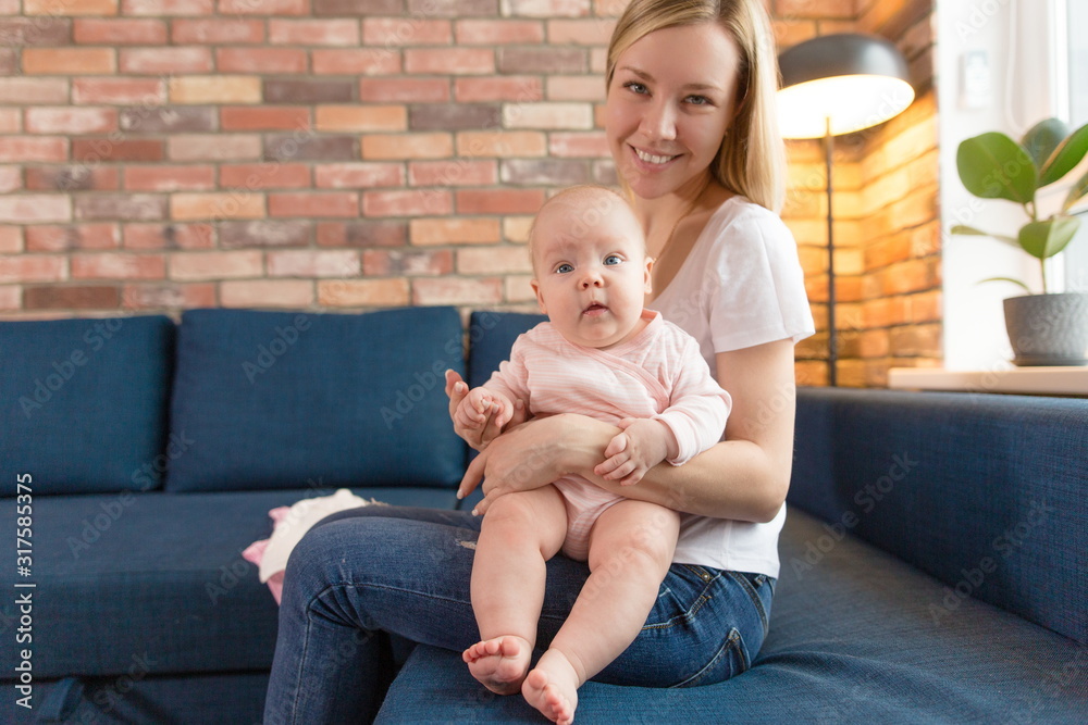 Young beautiful mother holding a baby on her lap sitting on the sofa in ...