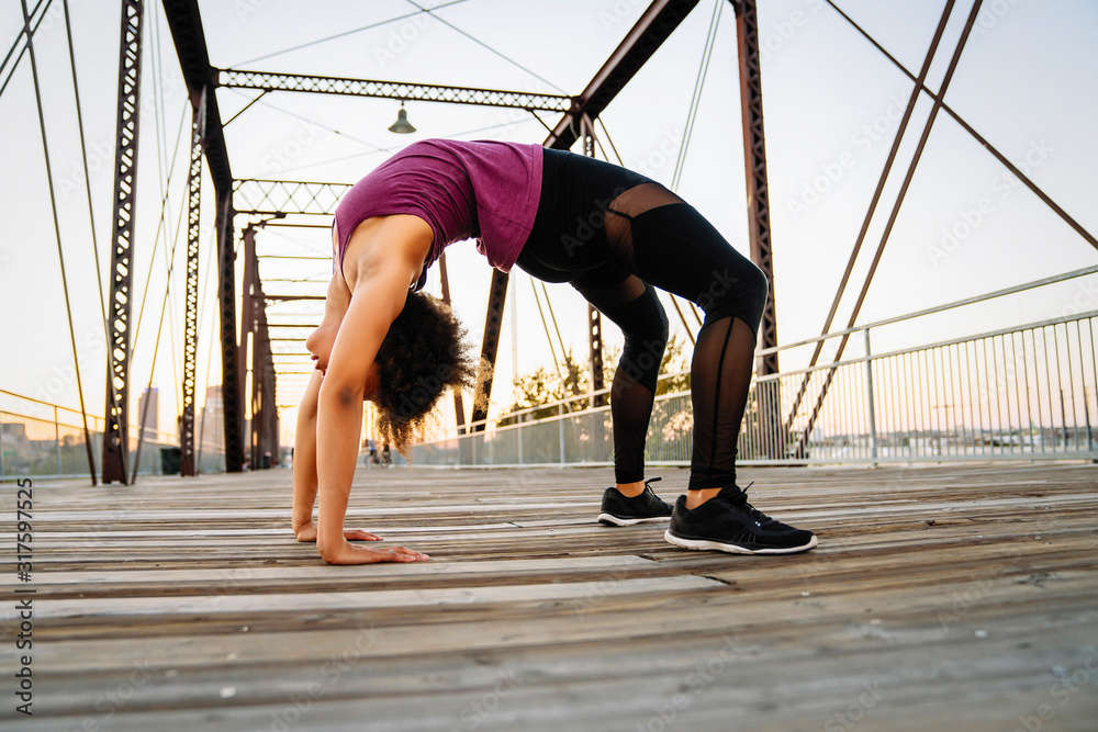 Woman in fitness attire on pedestrian bridge in city doing back bend ...