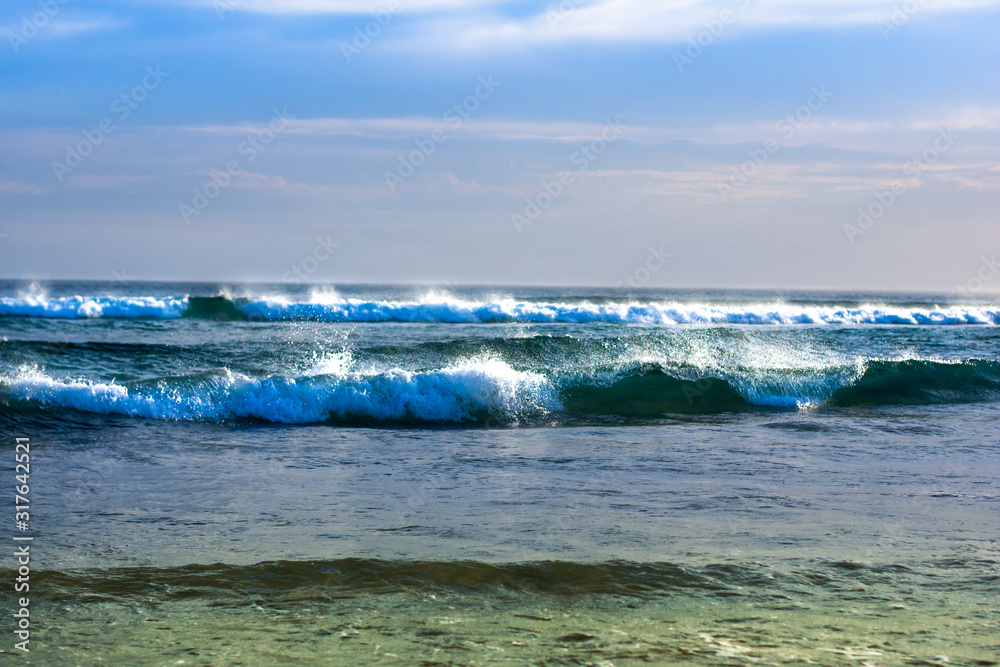 Two low ocean waves, rushing on the shore. Foam on the ridges glows in ...