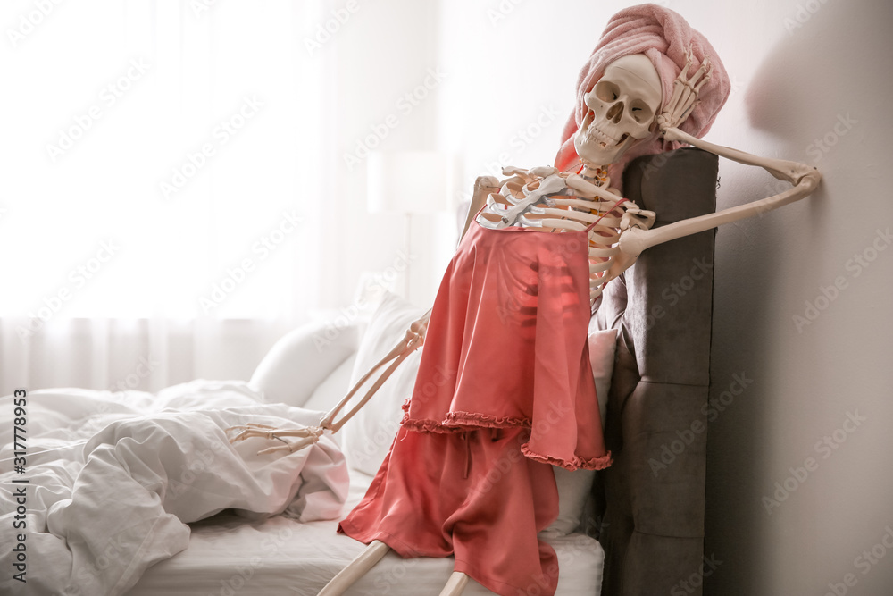 Human skeleton in silk pajamas and towel sitting on bed indoors Stock ...