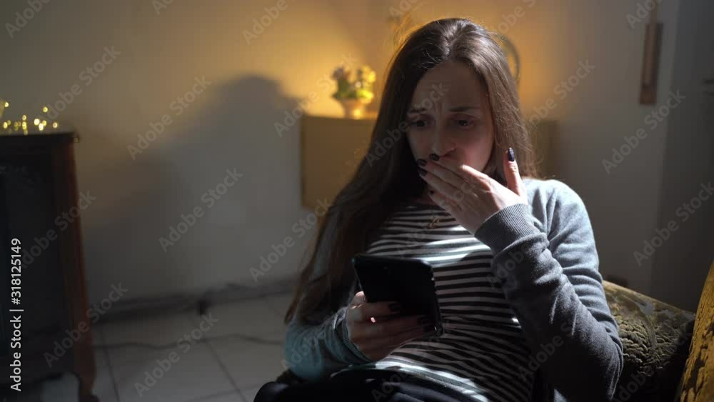 Scared girl sitting on armchair and looking on cellphone display in a ...