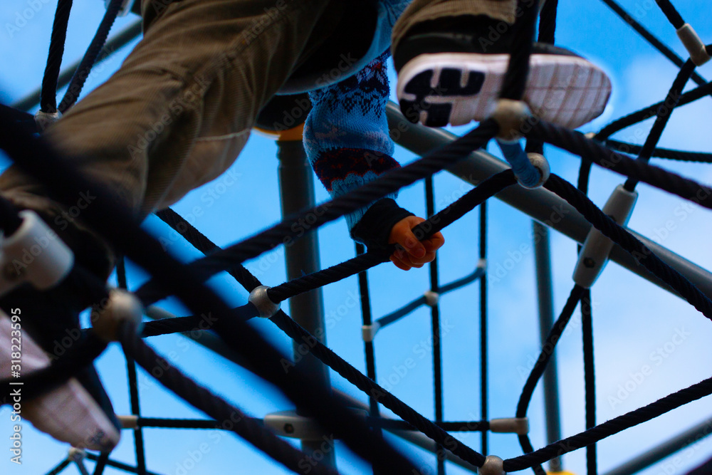 A boy on the playground climbing on a rope-ladder (web). A view of legs ...
