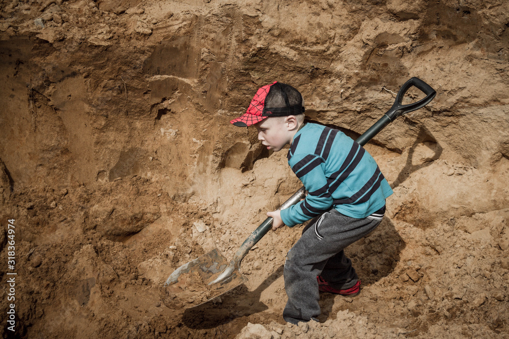 The boy is digging a deep pit in the sand. House construction. Stock ...
