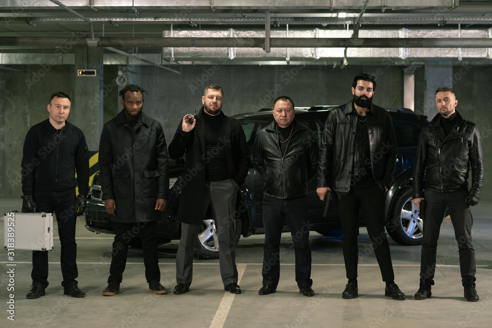 Row of intercultural armed gangsters or criminals in black jackets and ...