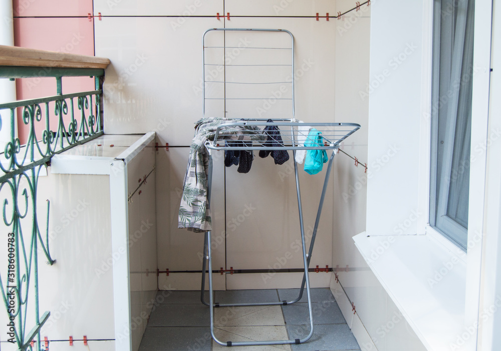 Metal drying rack stands on the balcony, wet clothes are drying and ...