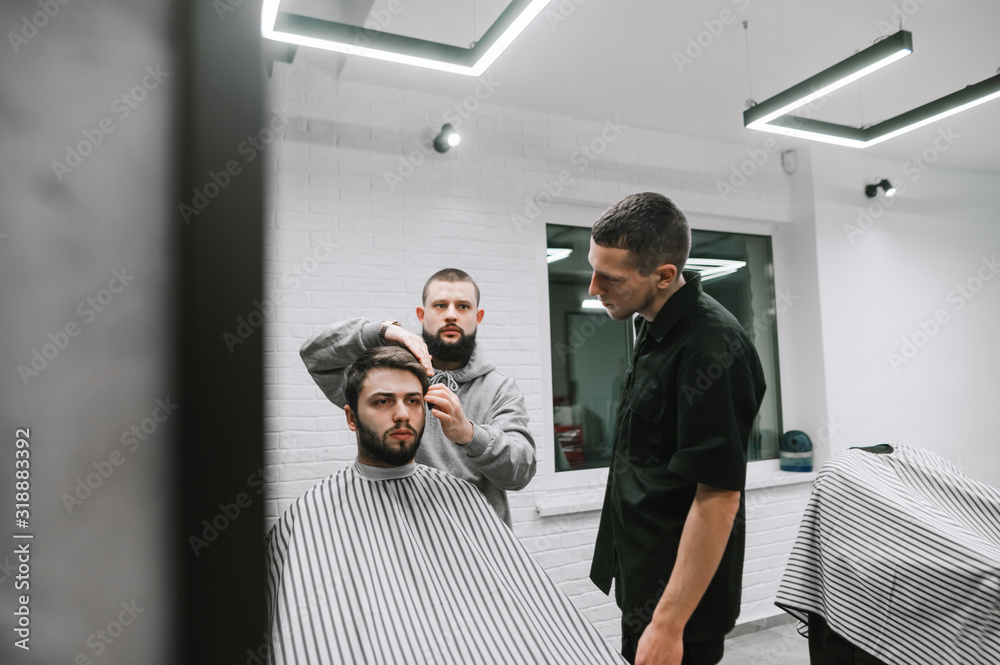 Two barbers create hairstyle for bearded man in bright modern ...